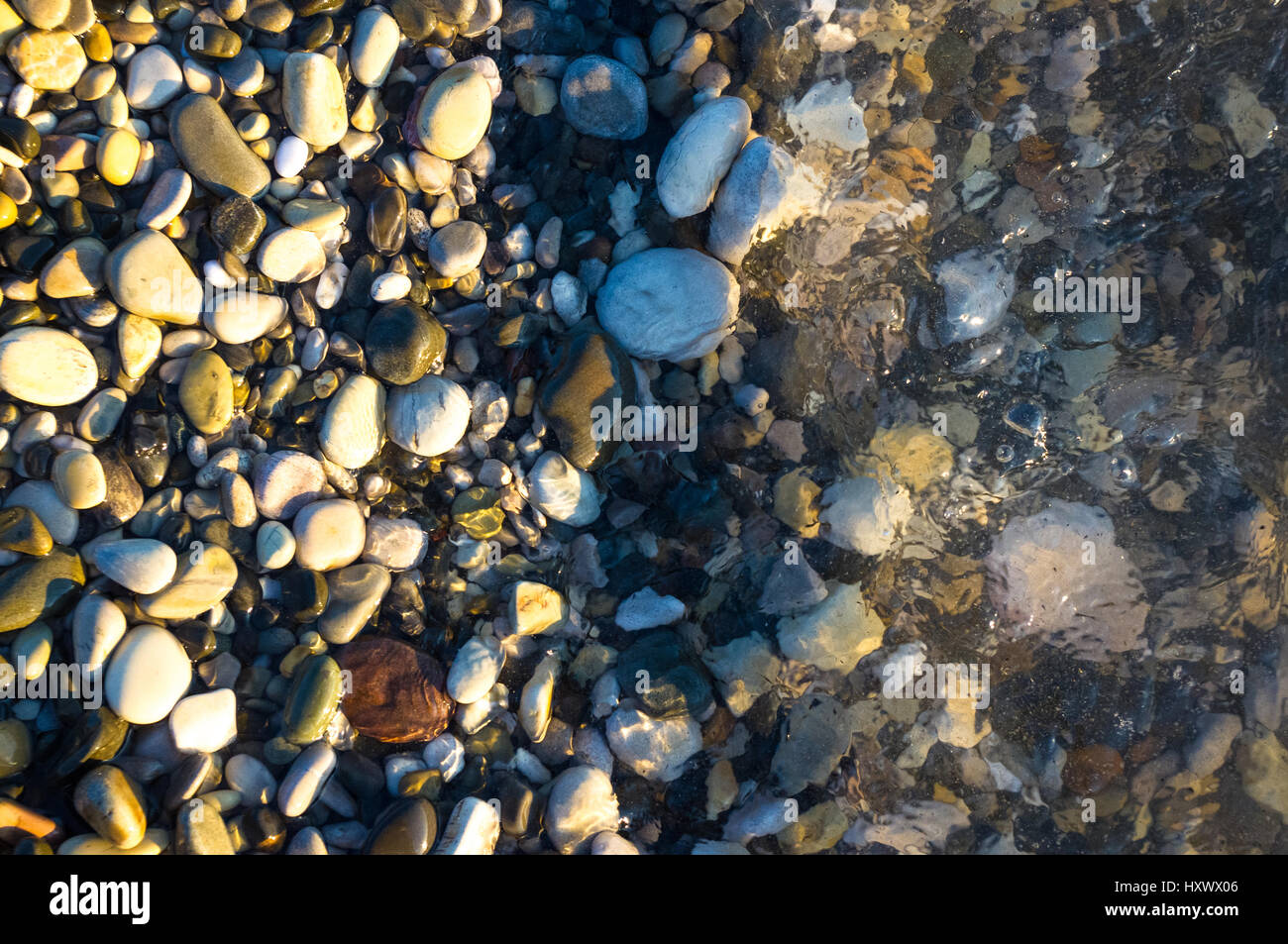 sea pebble beach with multicoloured stones, transparent waves with foam ...