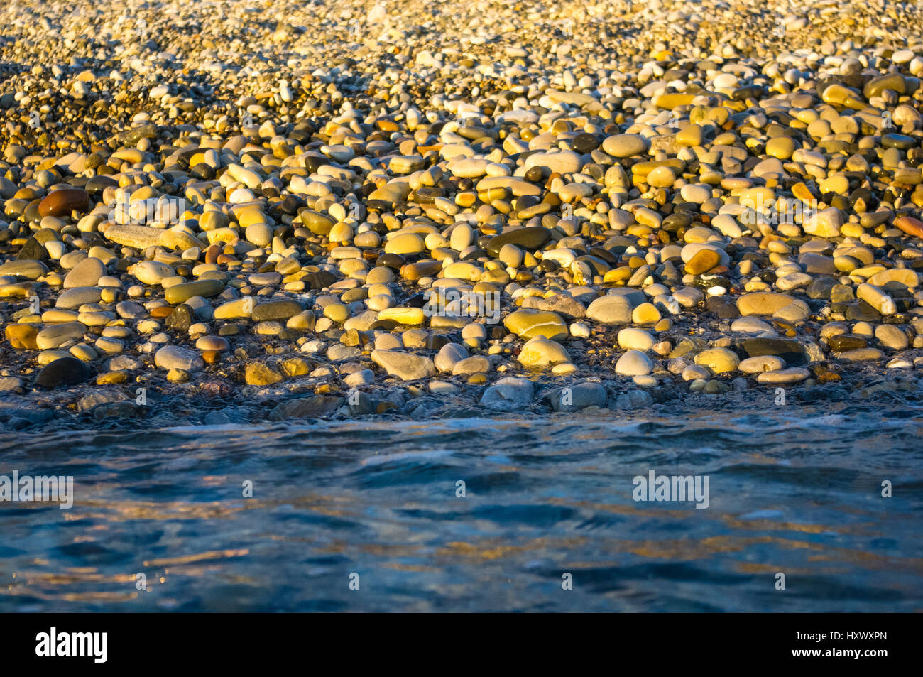 sea pebble beach with multicoloured stones, transparent waves with foam ...