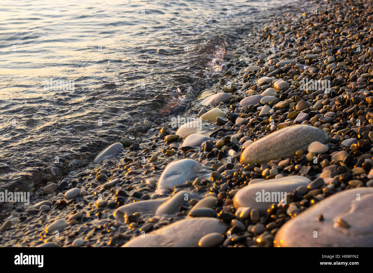 sea pebble beach with multicoloured stones, transparent waves with foam ...