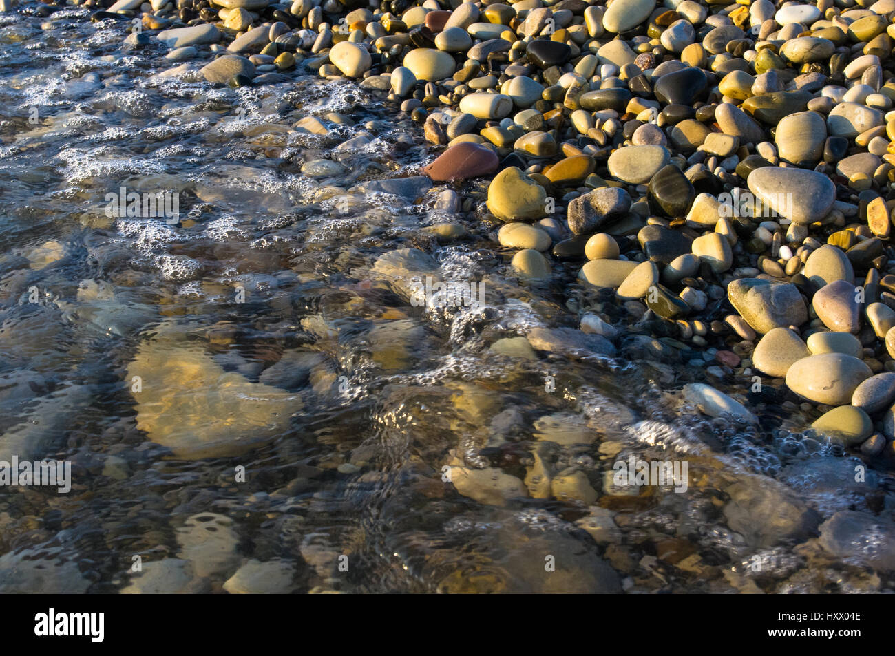 sea pebble beach with multicoloured stones, transparent waves with foam ...