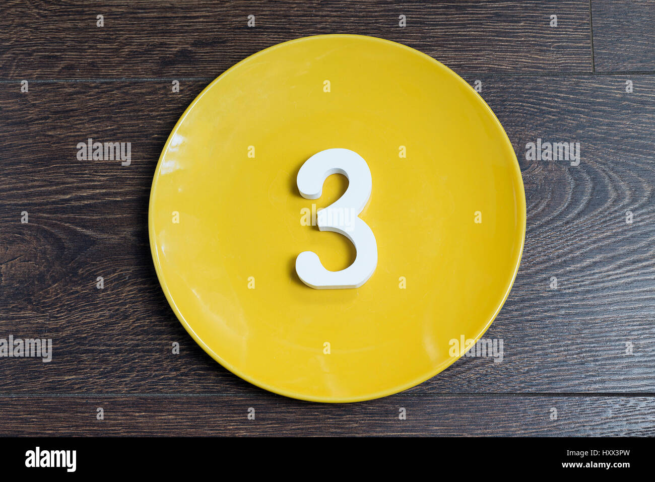 Number three on the yellow plate and brown background Stock Photo - Alamy
