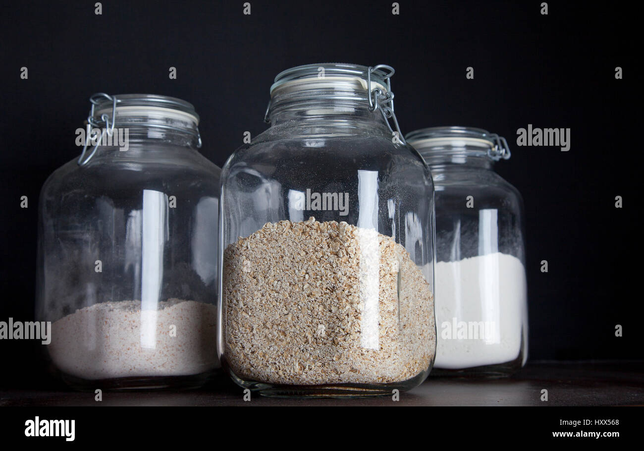 Three huge glass jars with oatmeal and flower on dark black background ...