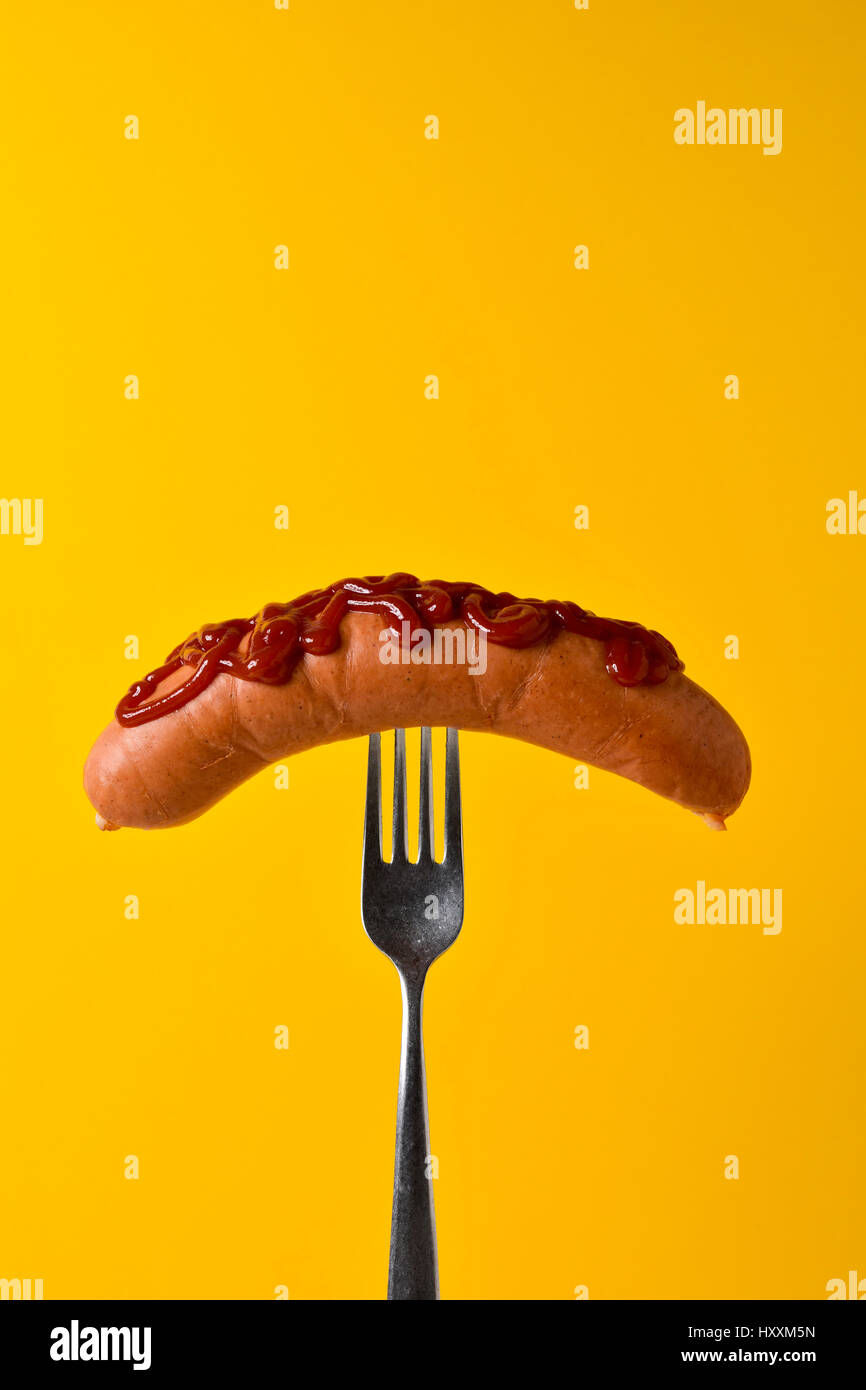 a hot dog topped with ketchup and curved down, as a sad face, in a fork ...