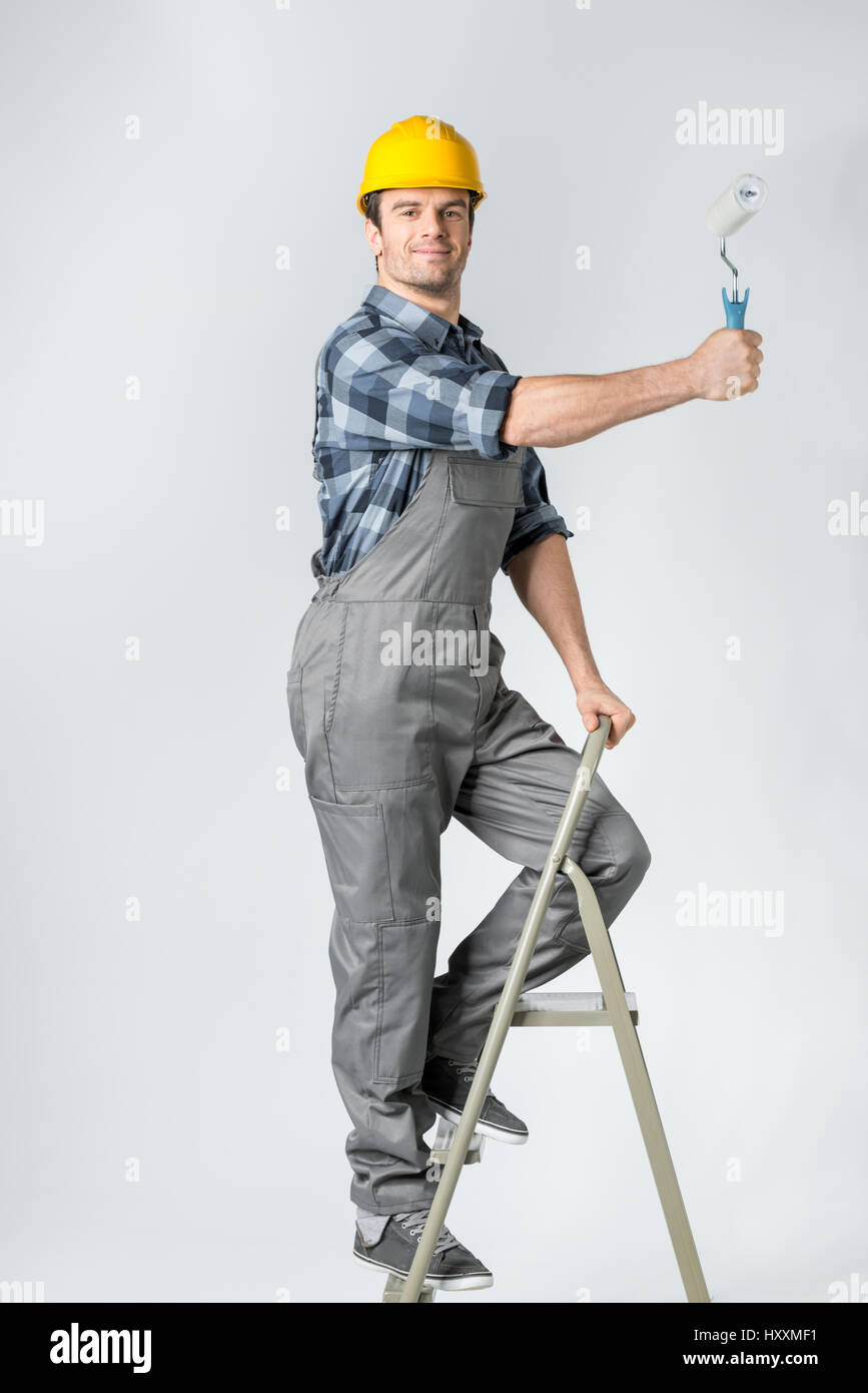 Smiling workman standing on ladder and painting wall with roller Stock ...