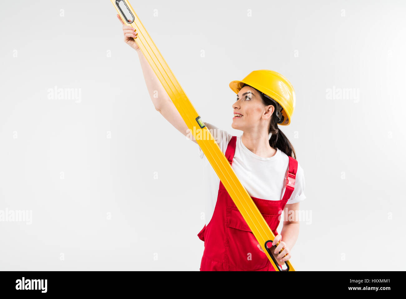 Smiling female engineer in helmet holding level tool on grey Stock ...