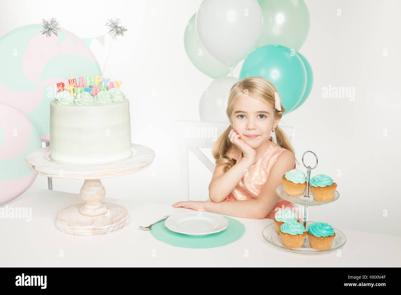 Smiling little girl sitting at table with birthday sweets Stock Photo ...