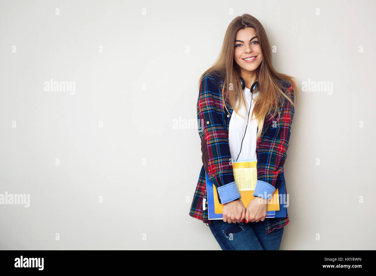 Studio portrait of young beautiful female student with books standing ...