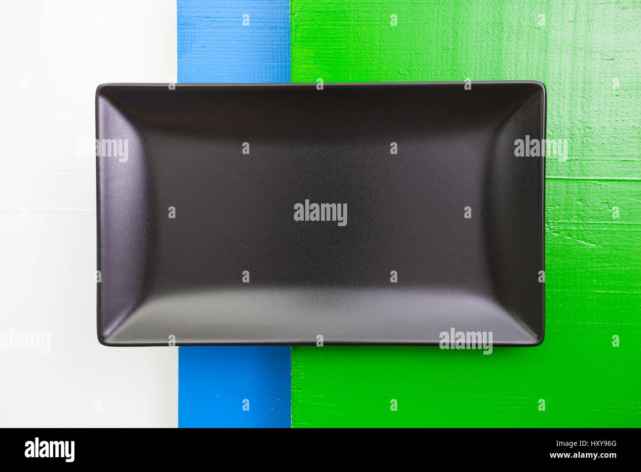 Black ceramic dish on over white, blue and green wooden table ...