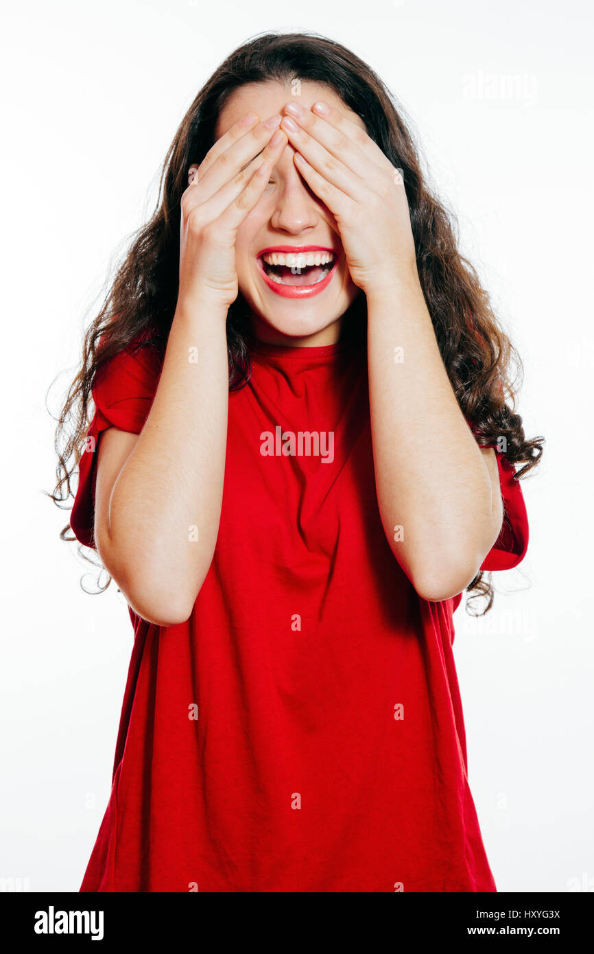 Portrait of surprised and laughing young woman covering eyes with hands ...