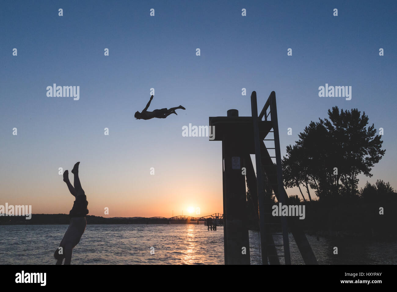 Two men dive from a platform into a large river at sunset. The Columbia ...
