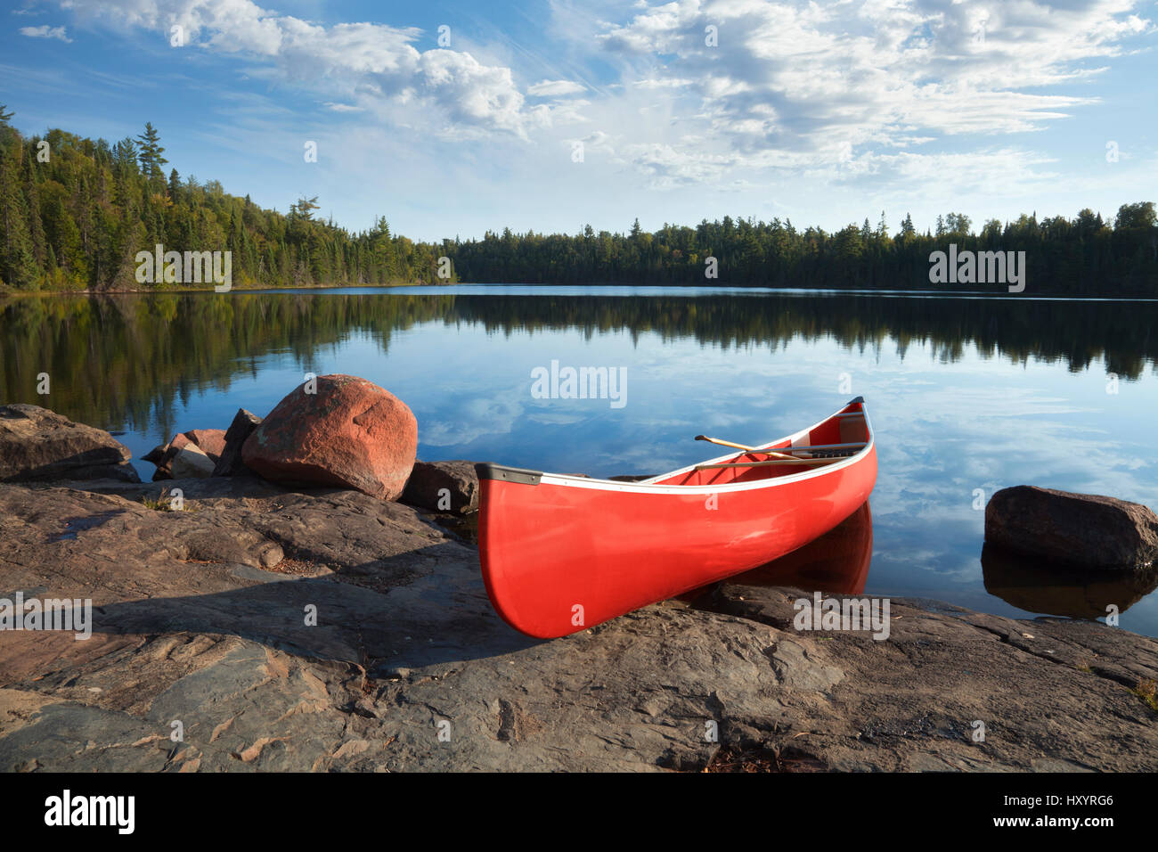 A yellow canoe rests on a rocky shore of a calm blue lake in the ...
