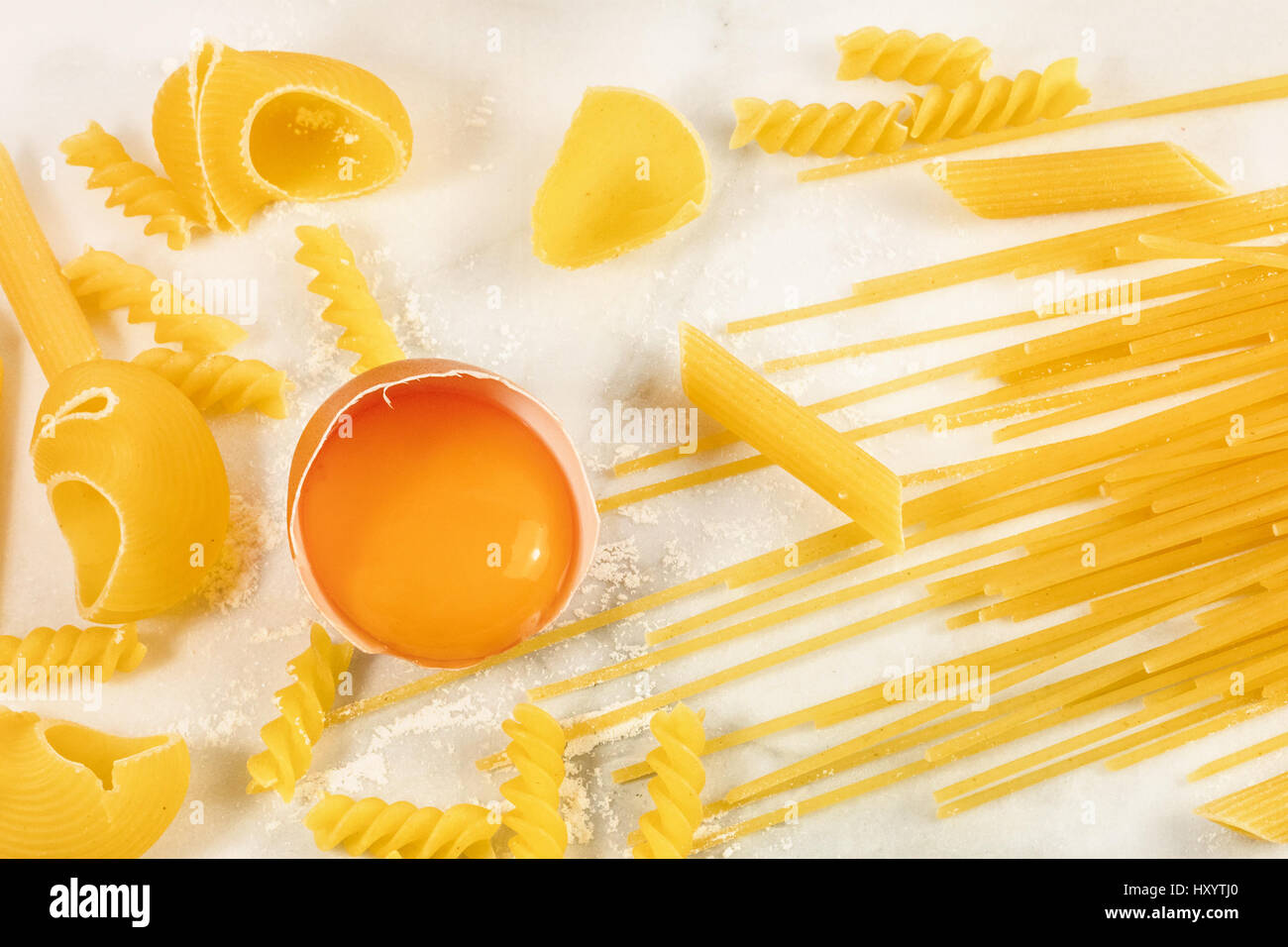 Various types of pasta on a white marble table with flour and an egg ...