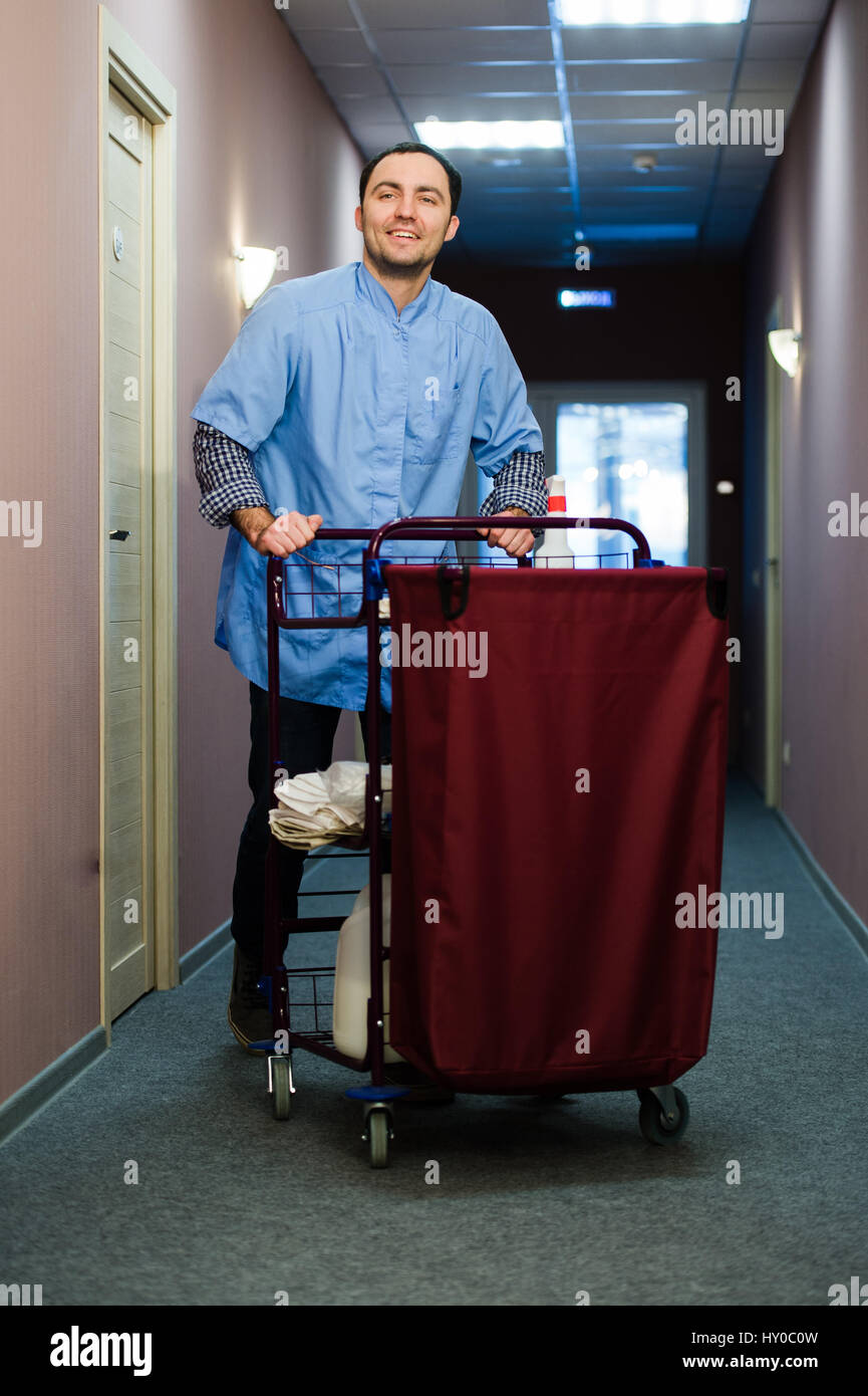 Young man pushing a housekeeping cart laden with clean towels, laundry ...