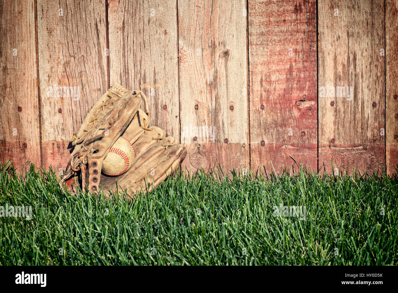 Old leather baseball mitt and ball on grass field against a rough ...