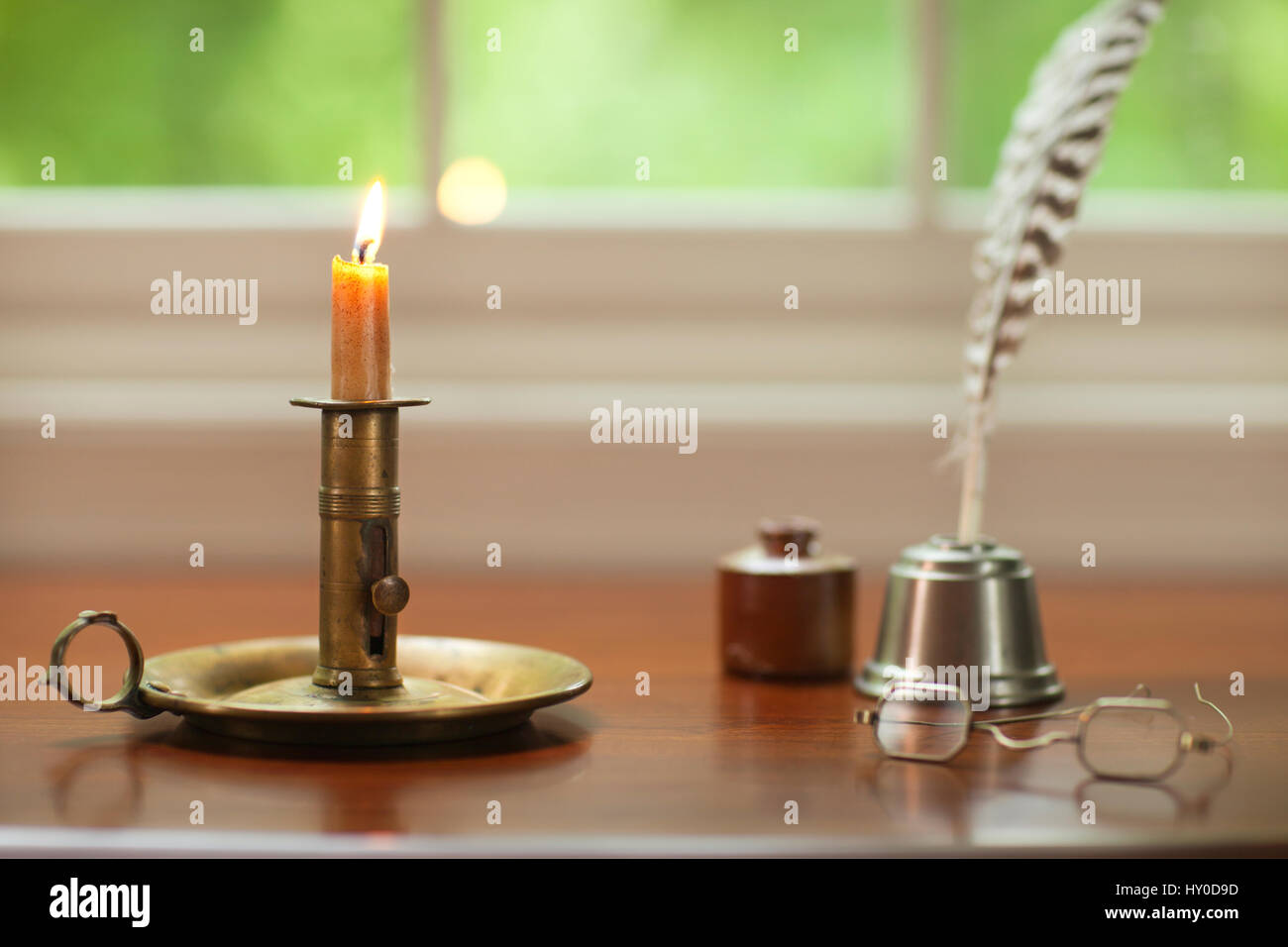 An colonial candle holder with a quill pen and glasses in front of a ...