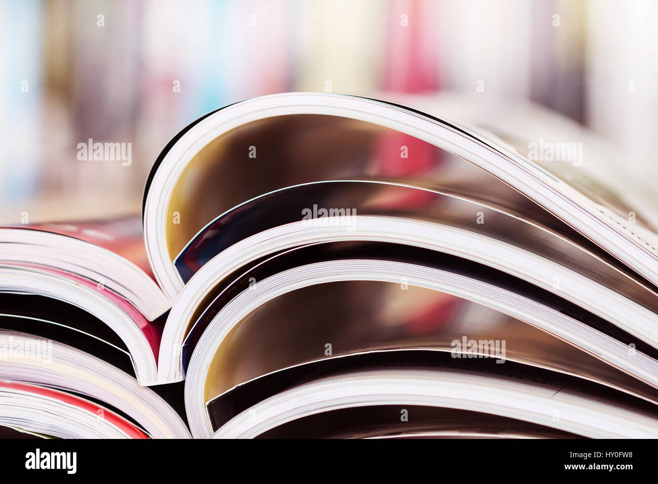 close up stacking of opened magazine with blurry bookshelf background ...