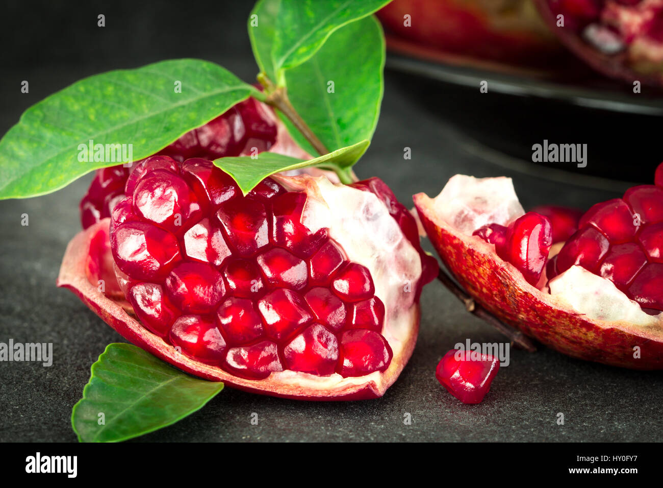 Fresh red pomegranate and seed with leaves over black stone background ...