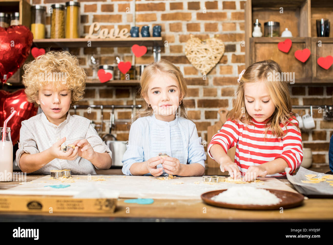 Three adorable little children cooking biscuits from unbaked dough ...