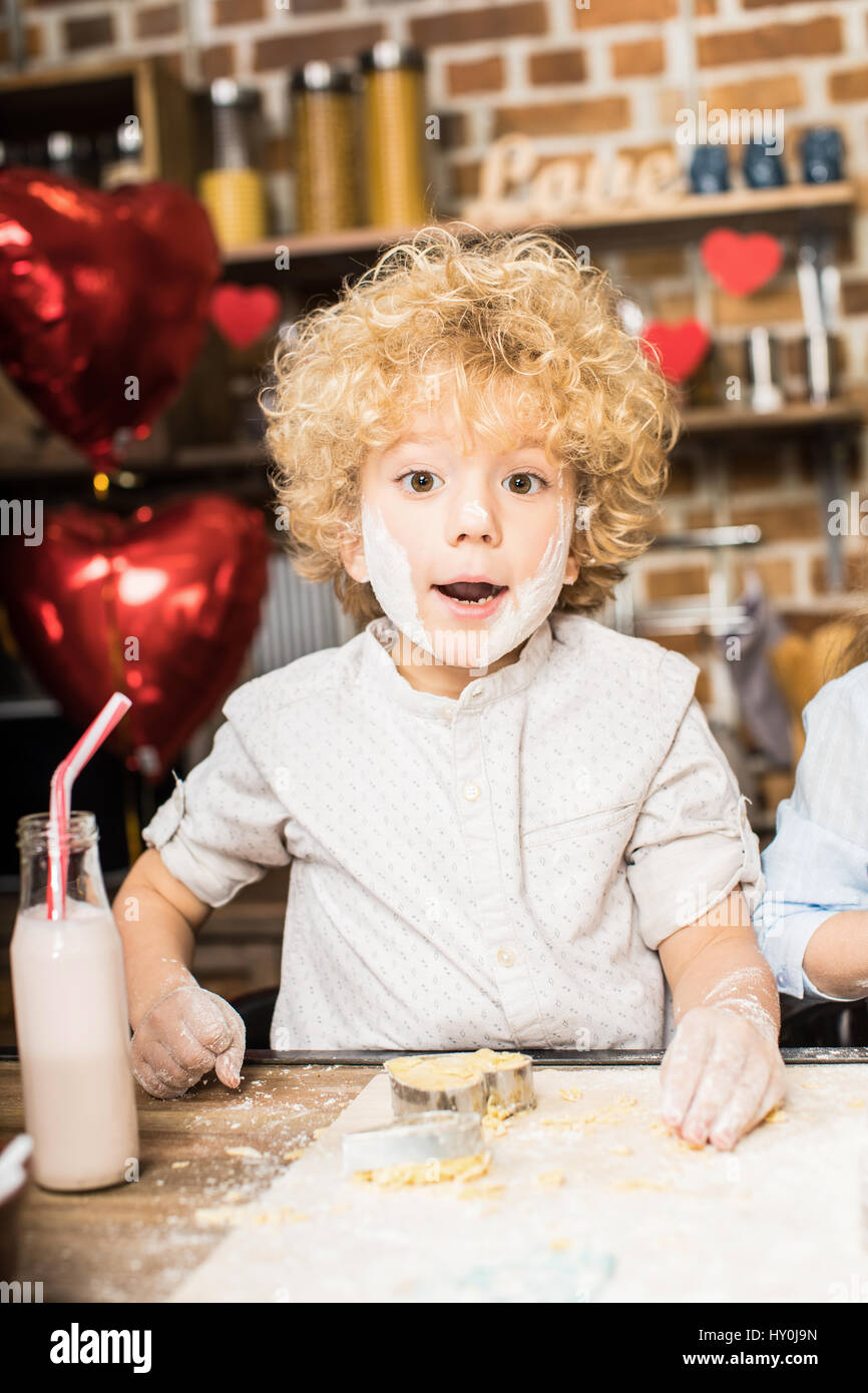 Portrait of exited little boy with flour-streaked face making cookies ...
