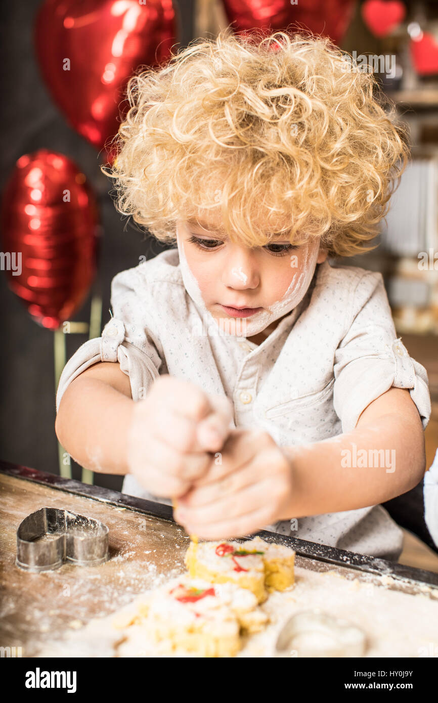 Portrait of curly little boy icing cookies for party Stock Photo - Alamy