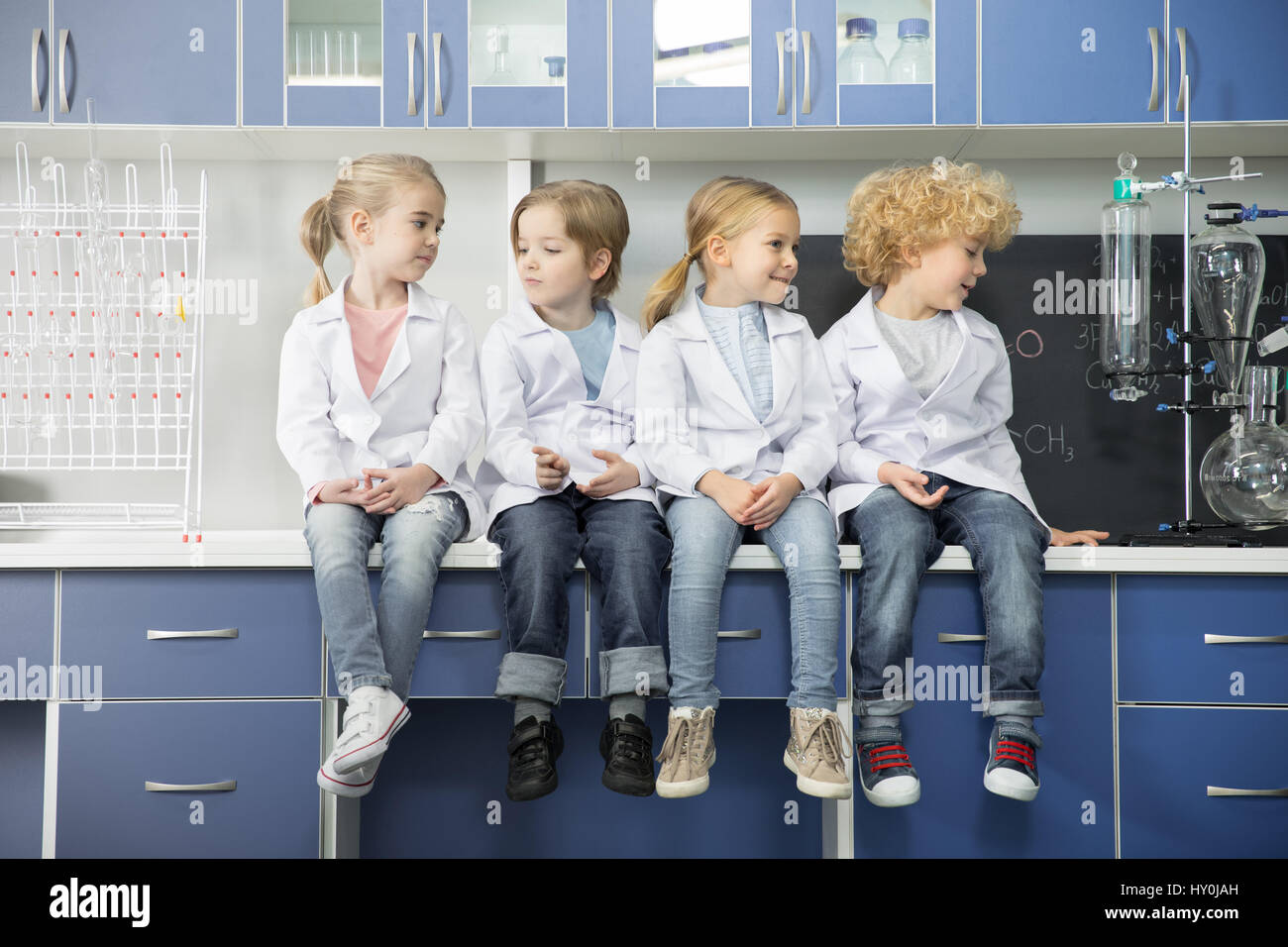 Schoolchildren in lab coats sitting together in chemical laboratory ...