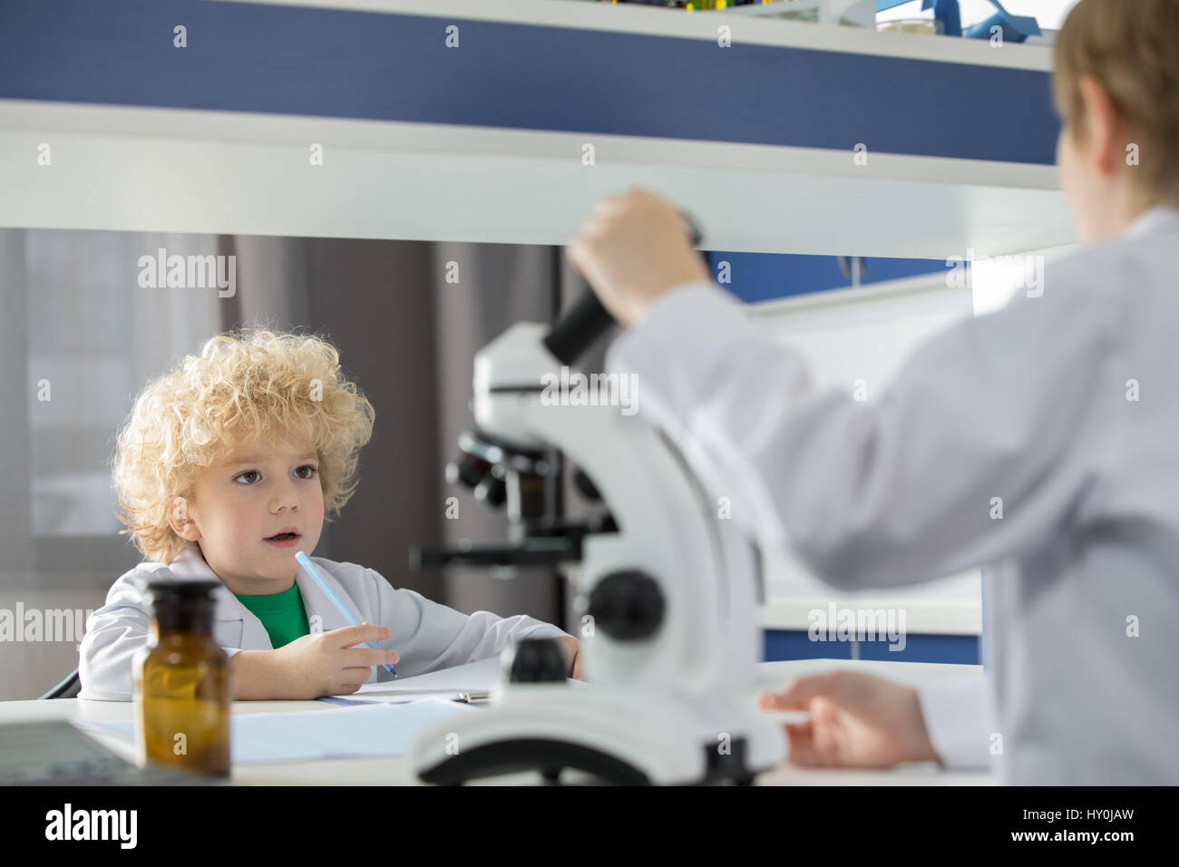 Schoolboy in white lab coat taking notes and looking at classmate Stock ...