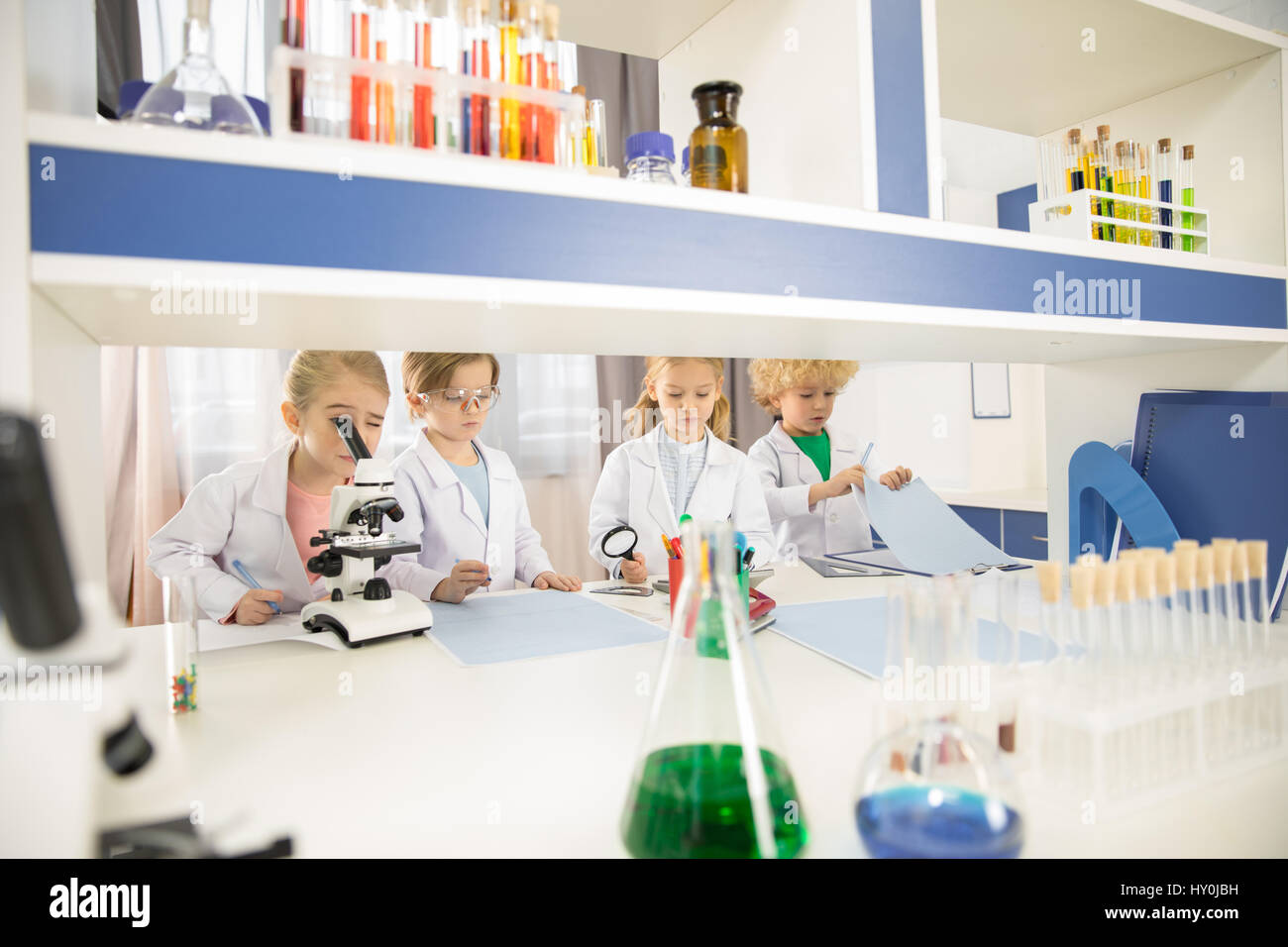 Schoolchildren in lab coats studying together in chemical laboratory ...
