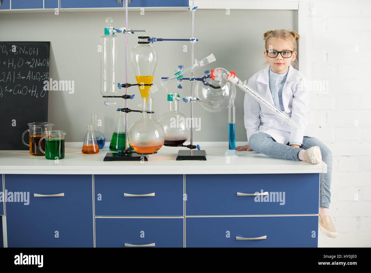 Little girl in white coat and eyeglasses sitting on table in science ...