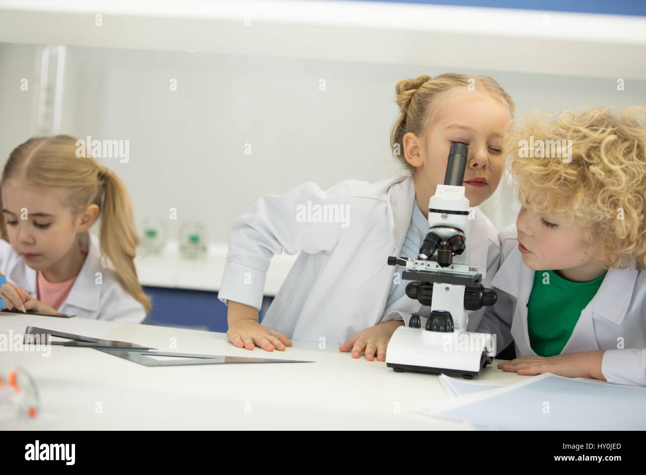 Little kids looking through microscope in science class Stock Photo - Alamy