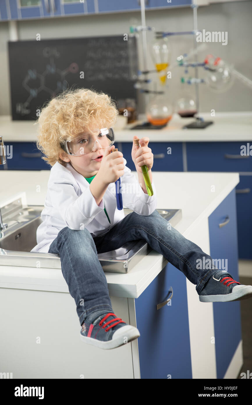 Little boy sitting in sink in science laboratory and holding test tubes ...