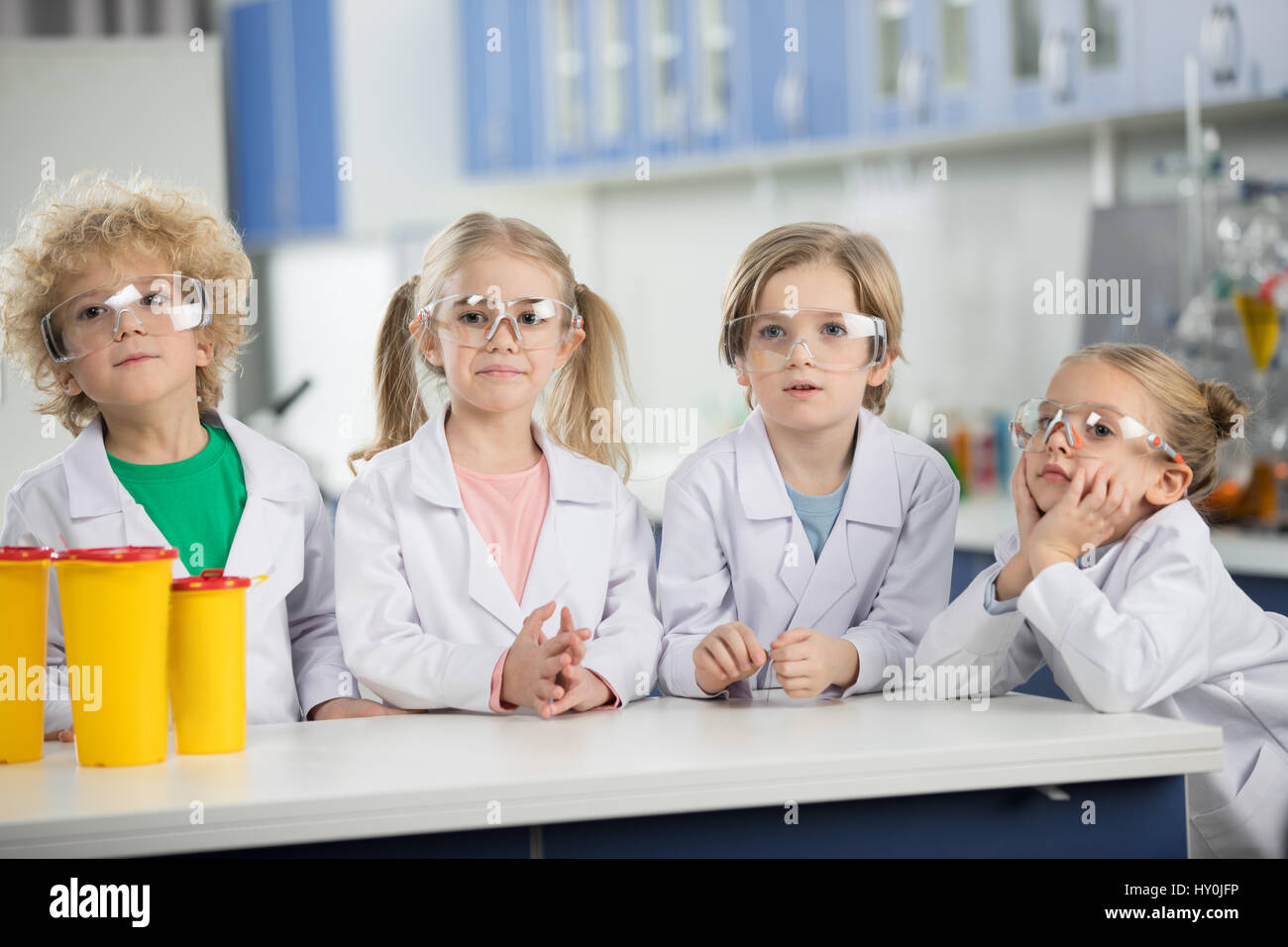 Four kids in science laboratory wearing coats and standing at table ...