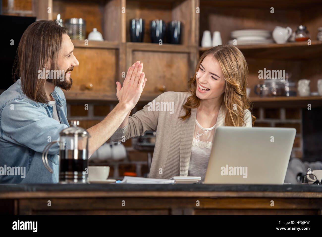Couple giving high five while working together with laptop at home ...