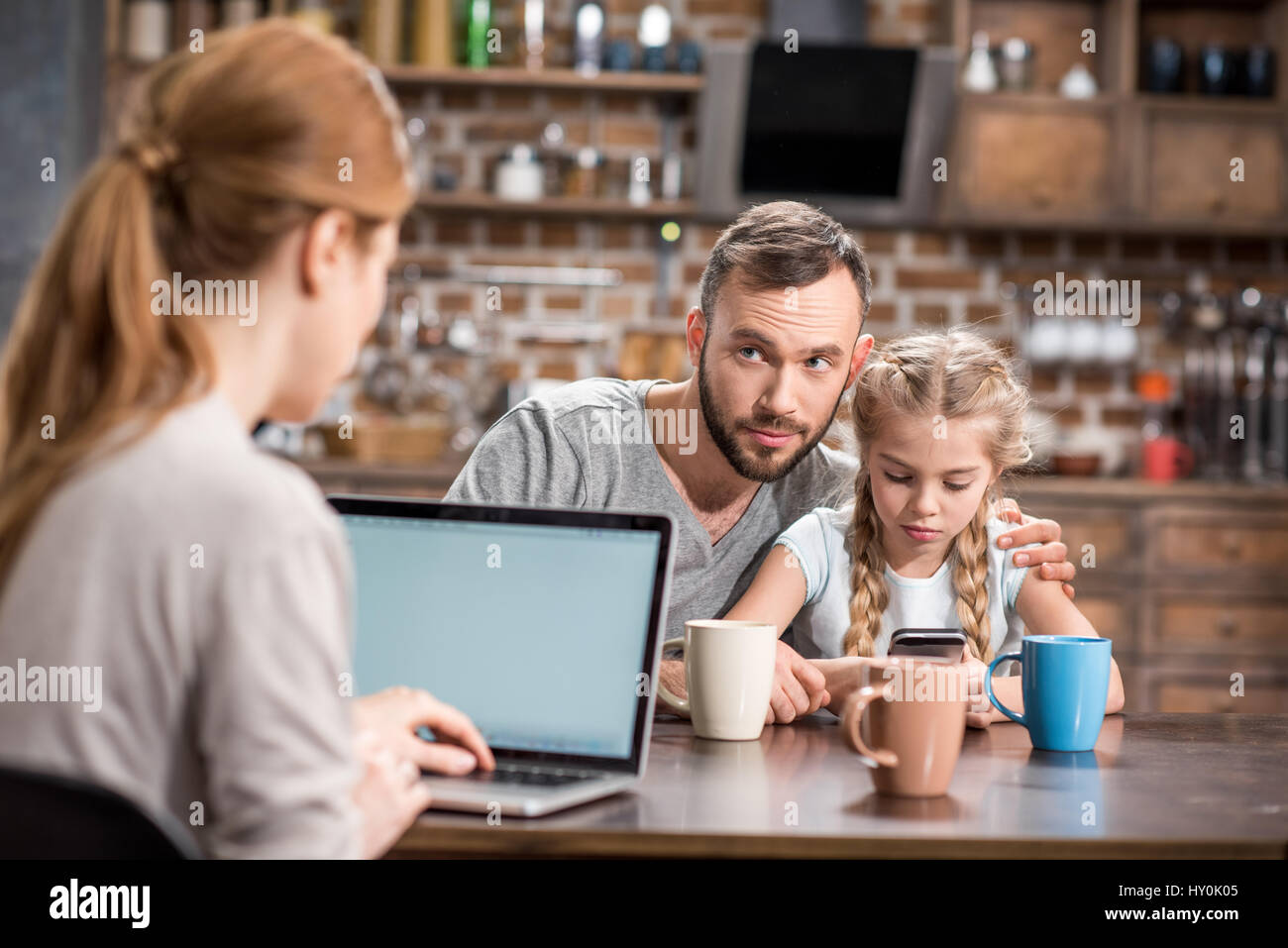 Young family in kitchen using devices and drinking tea or coffee Stock ...
