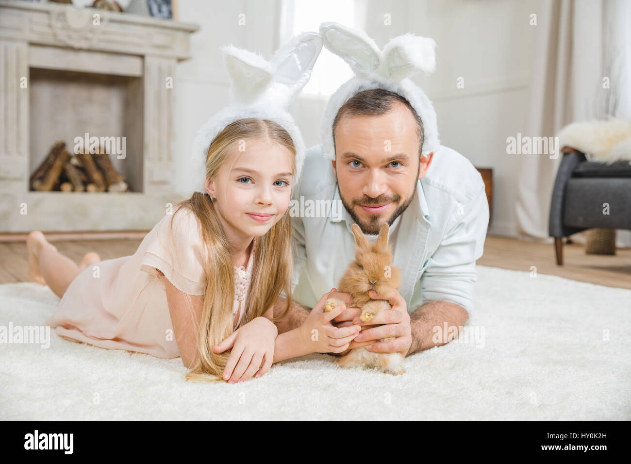 Happy father and daughter in bunny ears playing with rabbit at home ...