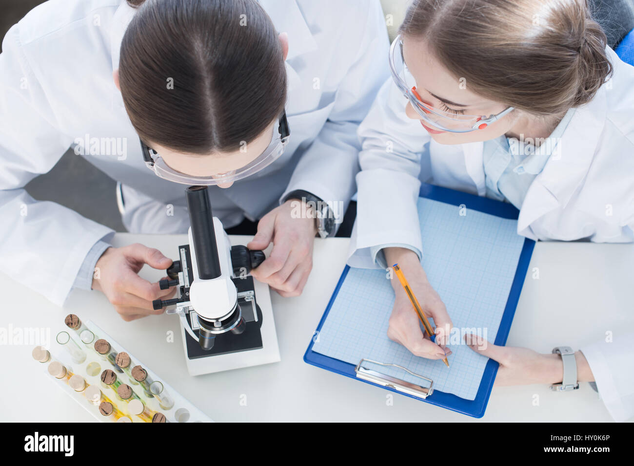 Overhead view of chemists working with microscope and taking notes in ...