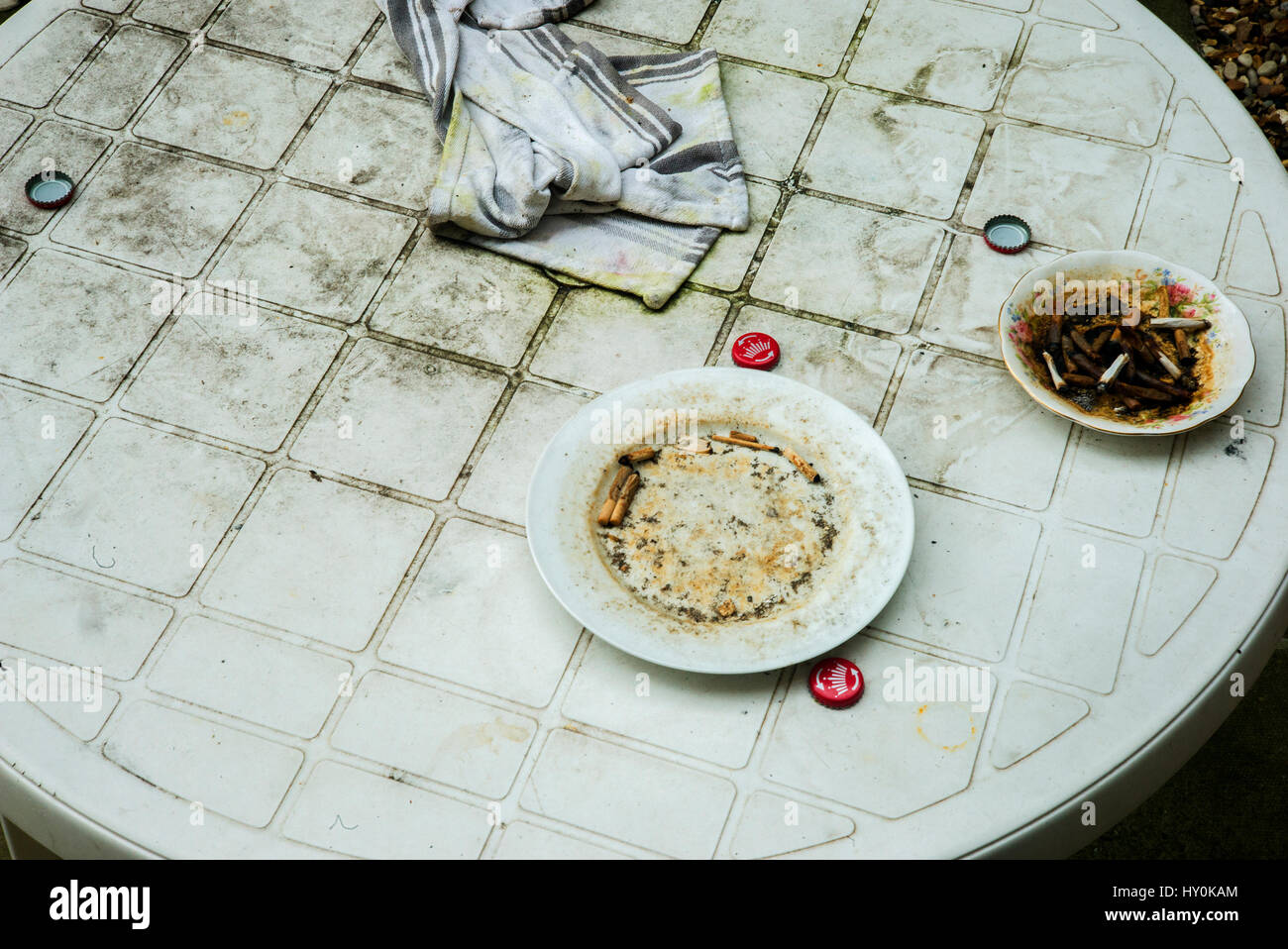 filthy garden table top with wet cloth and plates used as ashtrays ...