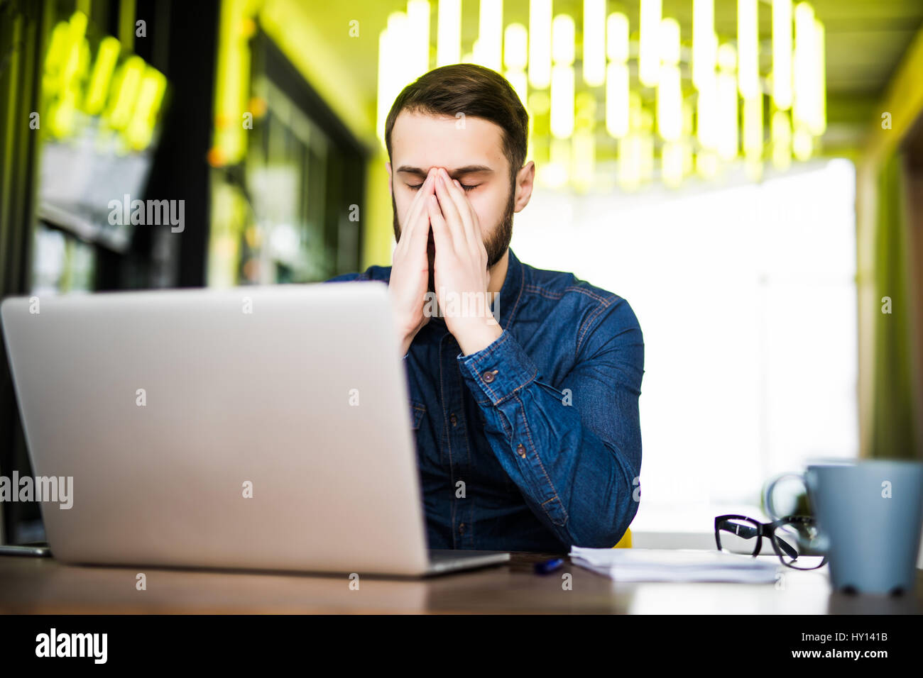 Picture of confused young man sitting near laptop and holding head with ...