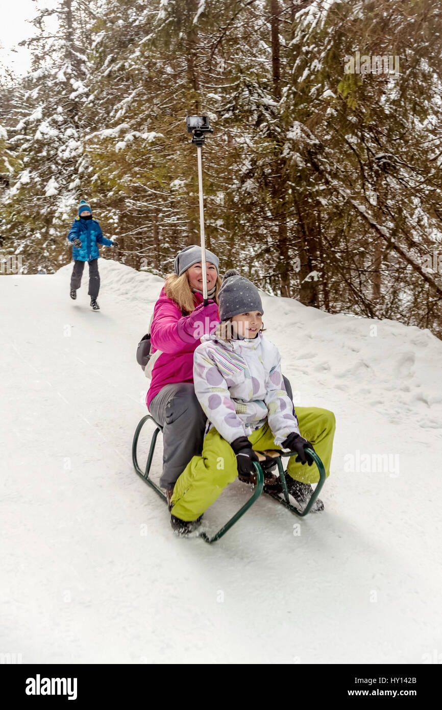 Woman filming with action camera while riding sled with her daughter ...