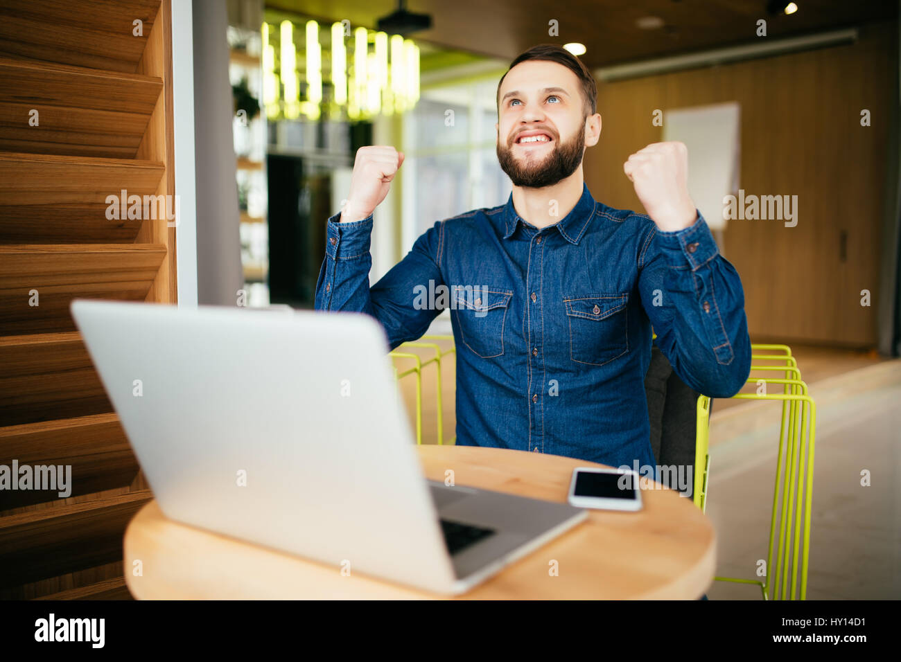 Happy excited young man sitting on workplace and celebrating success ...