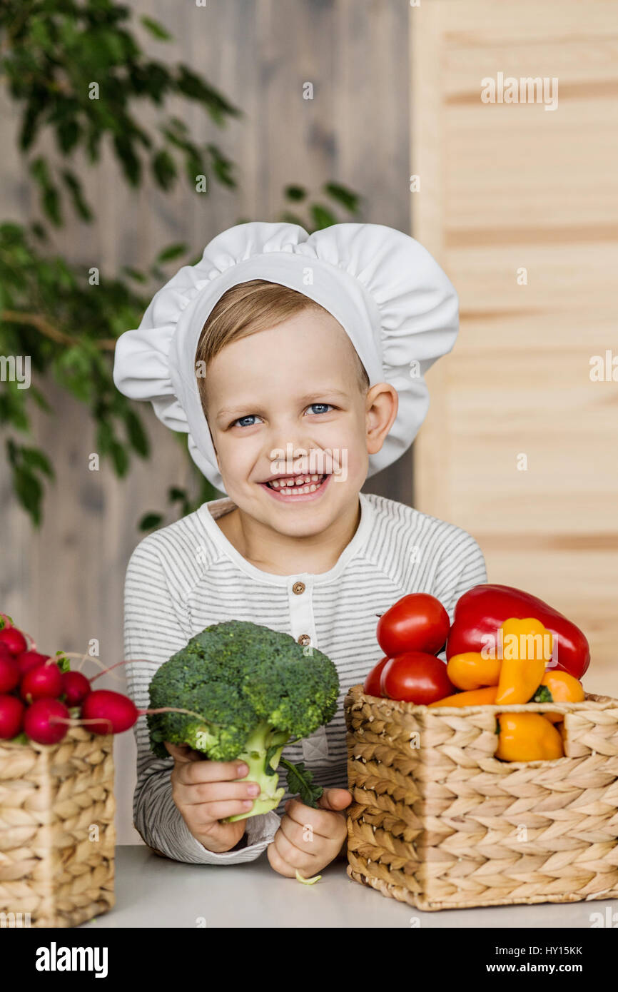 Handsome little kid in chef uniform with vegetables. Cooking in kitchen ...