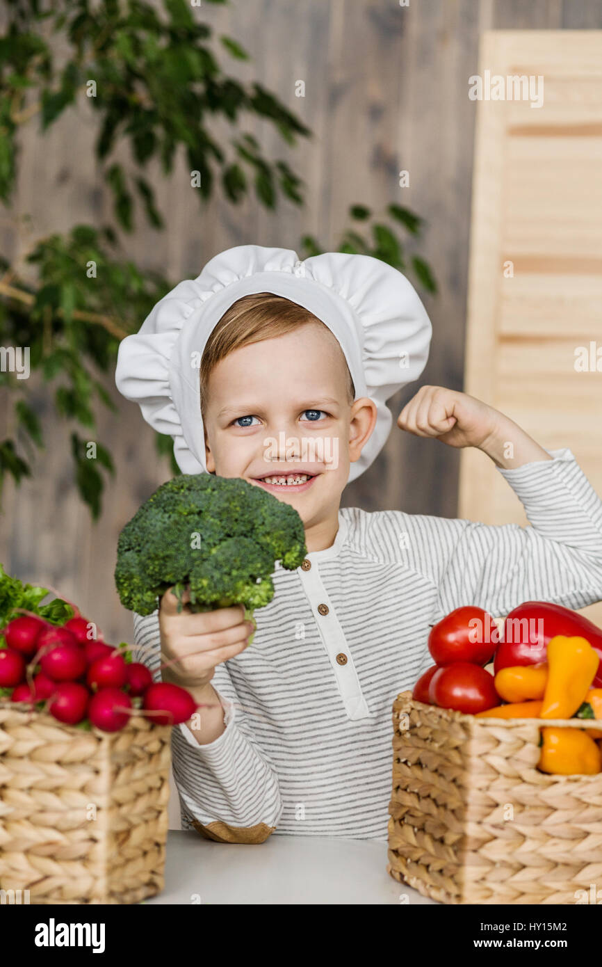 Handsome little kid in chef uniform with vegetables. Cooking in kitchen ...