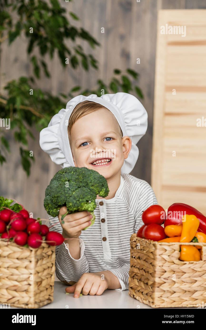 Handsome little kid in chef uniform with vegetables. Cooking in kitchen ...