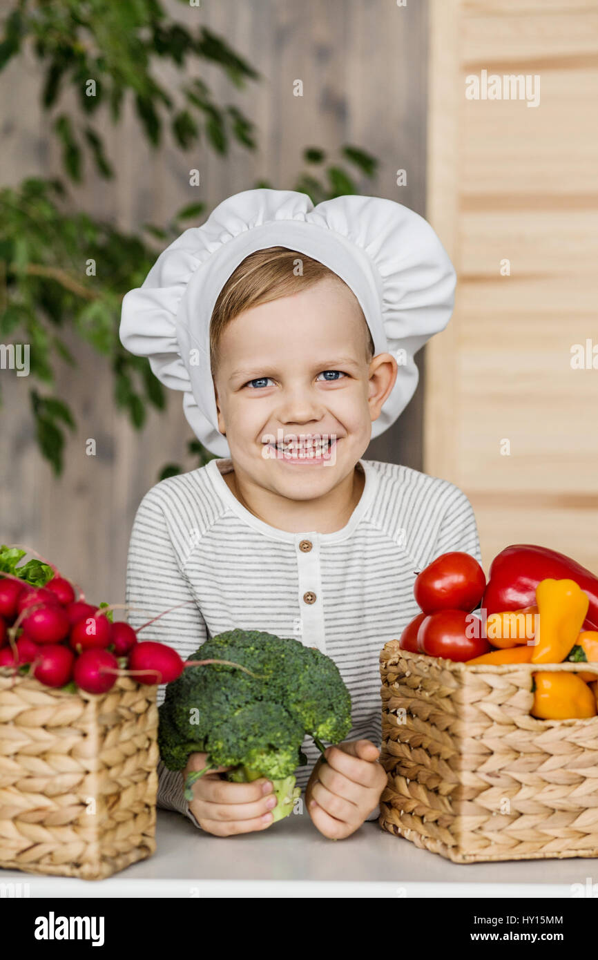 Handsome little kid in chef uniform with vegetables. Cooking in kitchen ...