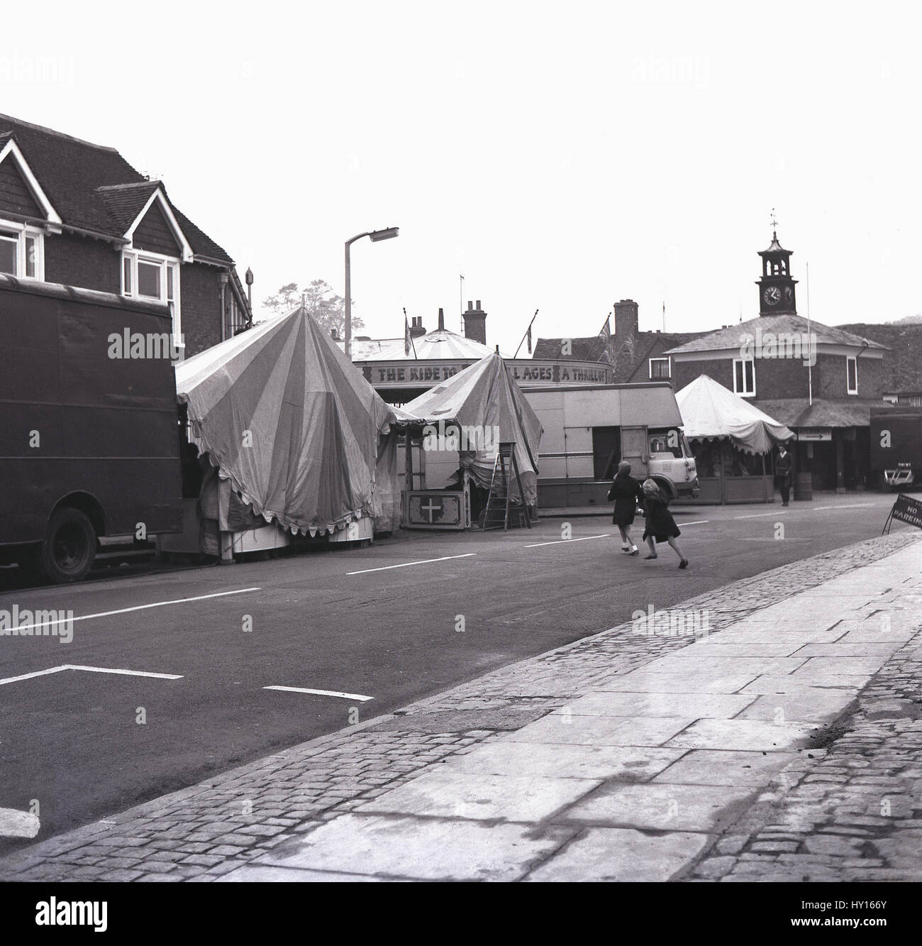 1960s, historical, two girls cross a quiet road to see the funfair that ...