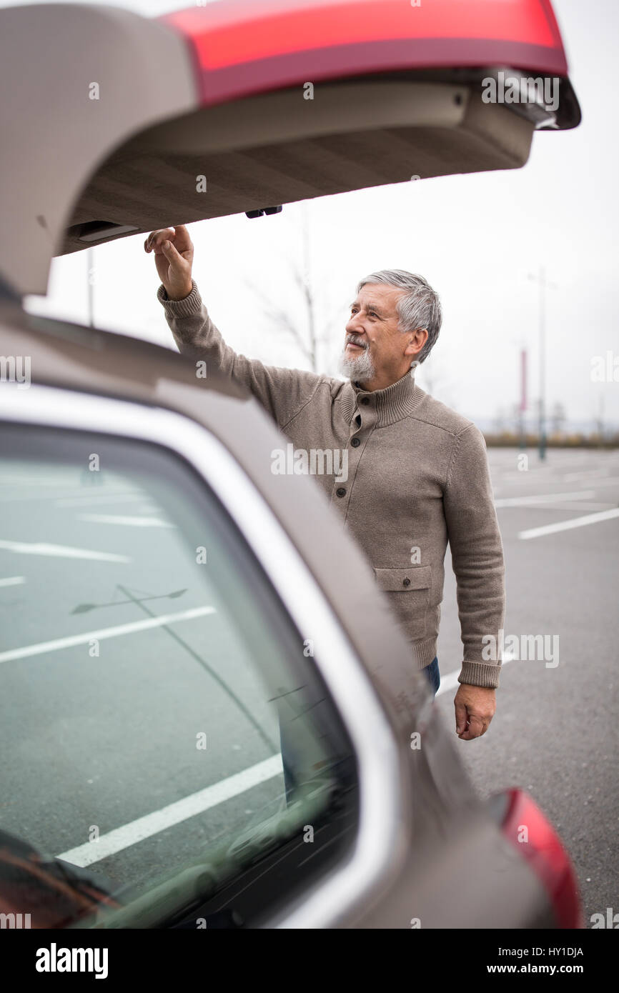 Senior man by his car, closing the trunk lid in a mall parking lot ...