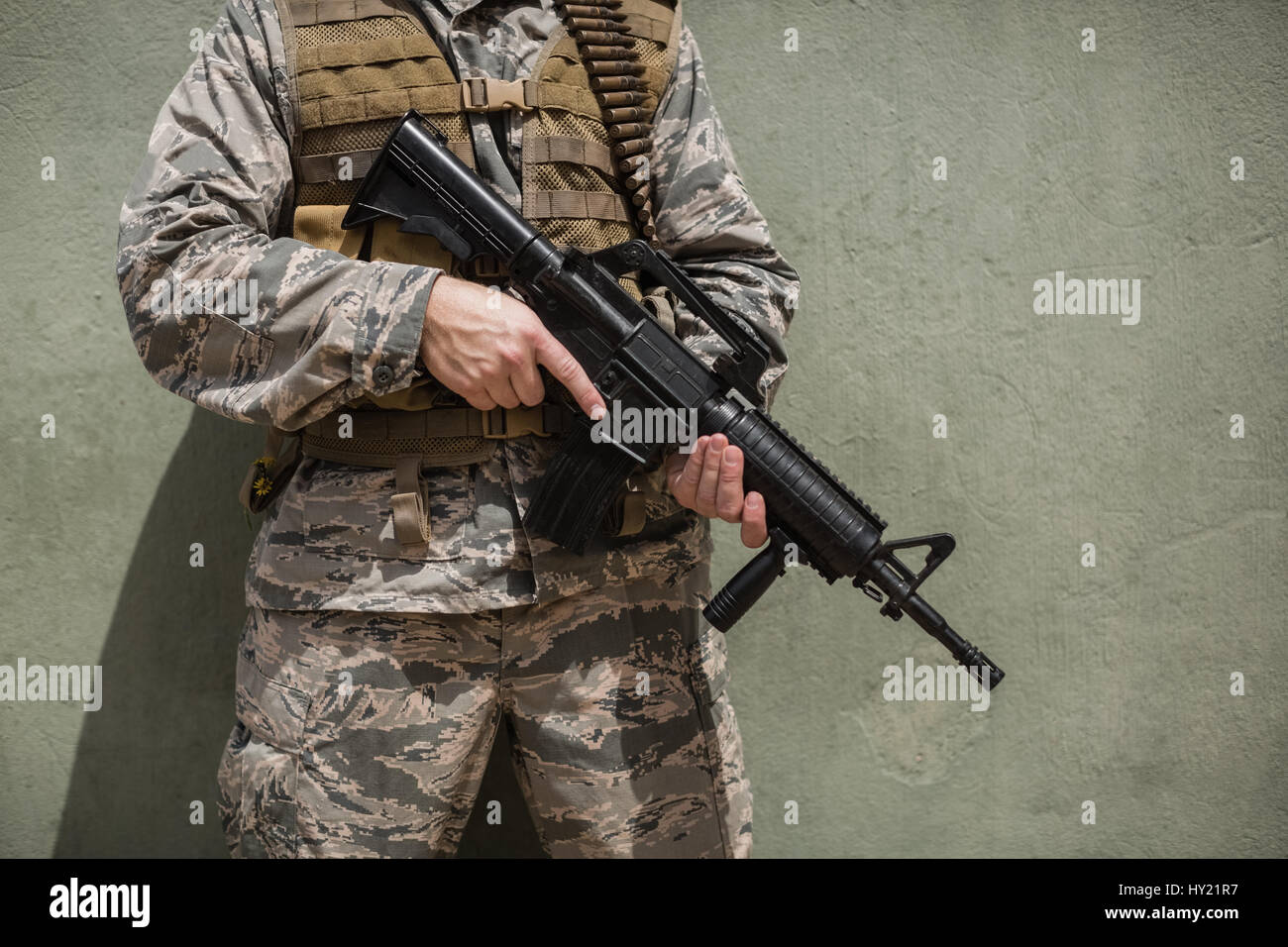Mid section of military soldier standing with a rifle against concrete ...