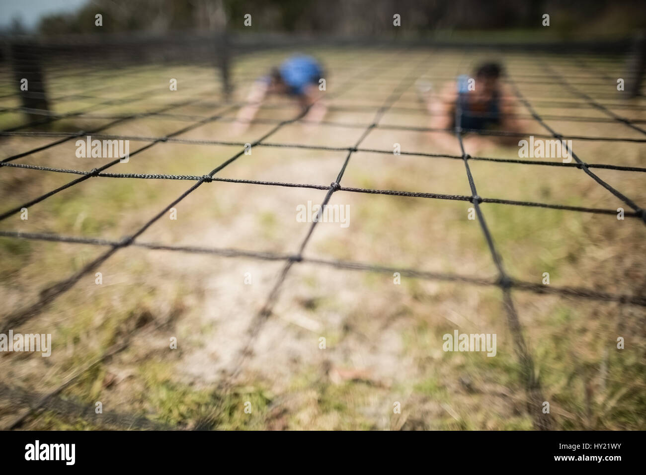 Fit man and woman crawling under the net during obstacle course in boot ...