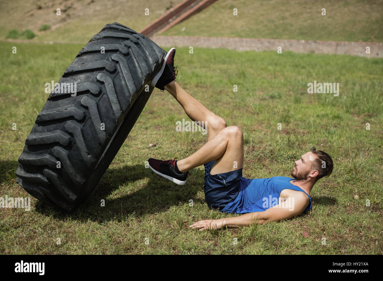 Fit man performing leg workout with tier during obstacle course in boot ...