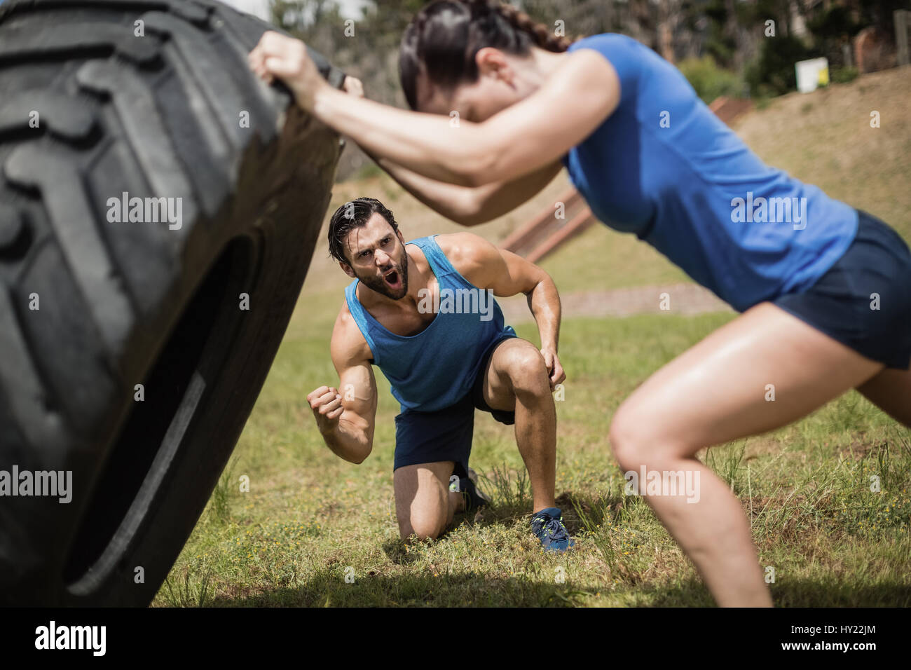 Fit woman flipping a tire while trainer cheering during obstacle course ...