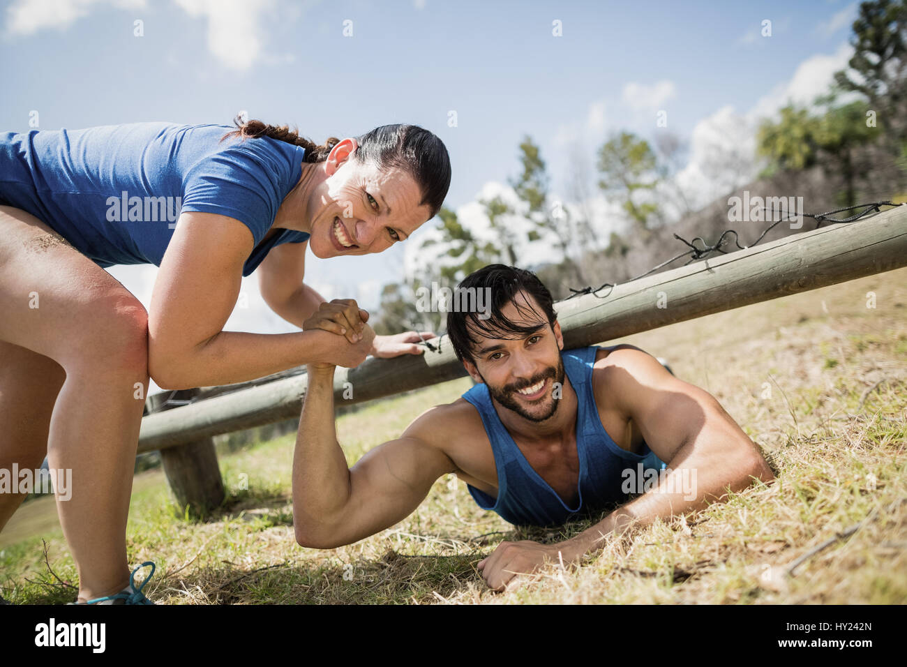 Smiling fit woman helping man crawling under the net during obstacle ...